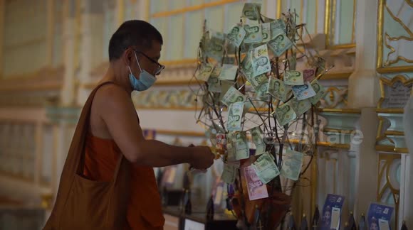 A Buddhist monk collects money from a money tree at a Thai temple ...