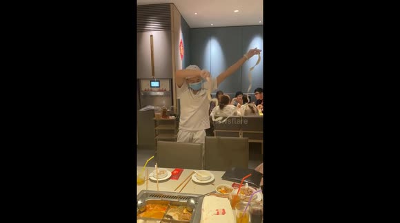 Enthusiastic restaurant worker dances while pulling one-strand noodle ...