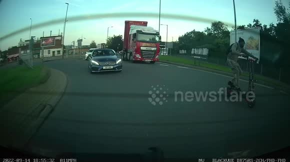 A man on Electric scooter filters through traffic on a busy roundabout ...