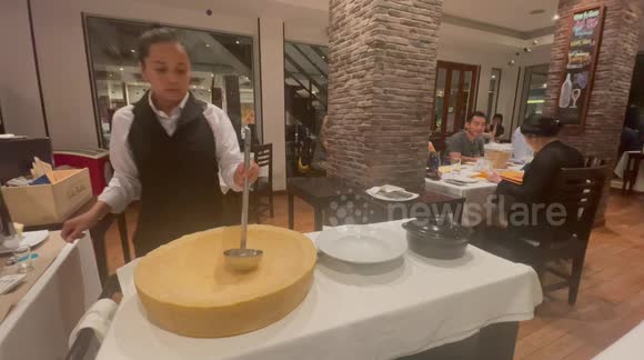 Waitress serves delicious pasta from flaming parmesan cheese wheel ...