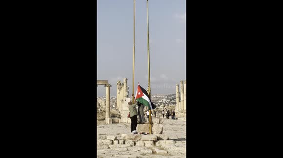 Two men raising the national flag of Jordan in Jerash Ruins. Jerash is ...